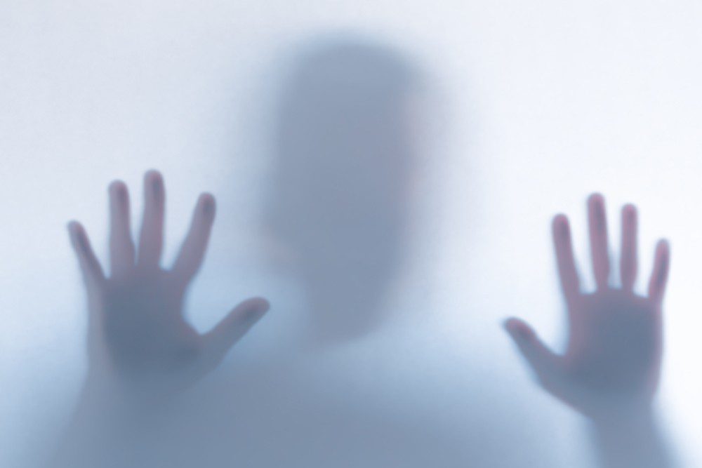 Defocused scary ghost silhouette behind a white glass background ...